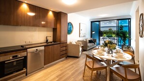 Cozinha moderna com armários de madeira e eletrodomésticos de aço inoxidável, área de jantar com mesa redonda e cadeiras, e uma grande porta de vidro deslizante que dá para uma varanda com plantas.