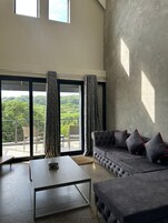 Uma sala de estar moderna com um sofá cinzento, uma mesa de centro e vista para o verde através de grandes janelas.