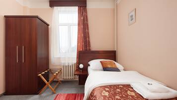 Quarto de hotel com cama, guarda-roupa, radiador e janela com cortinas.