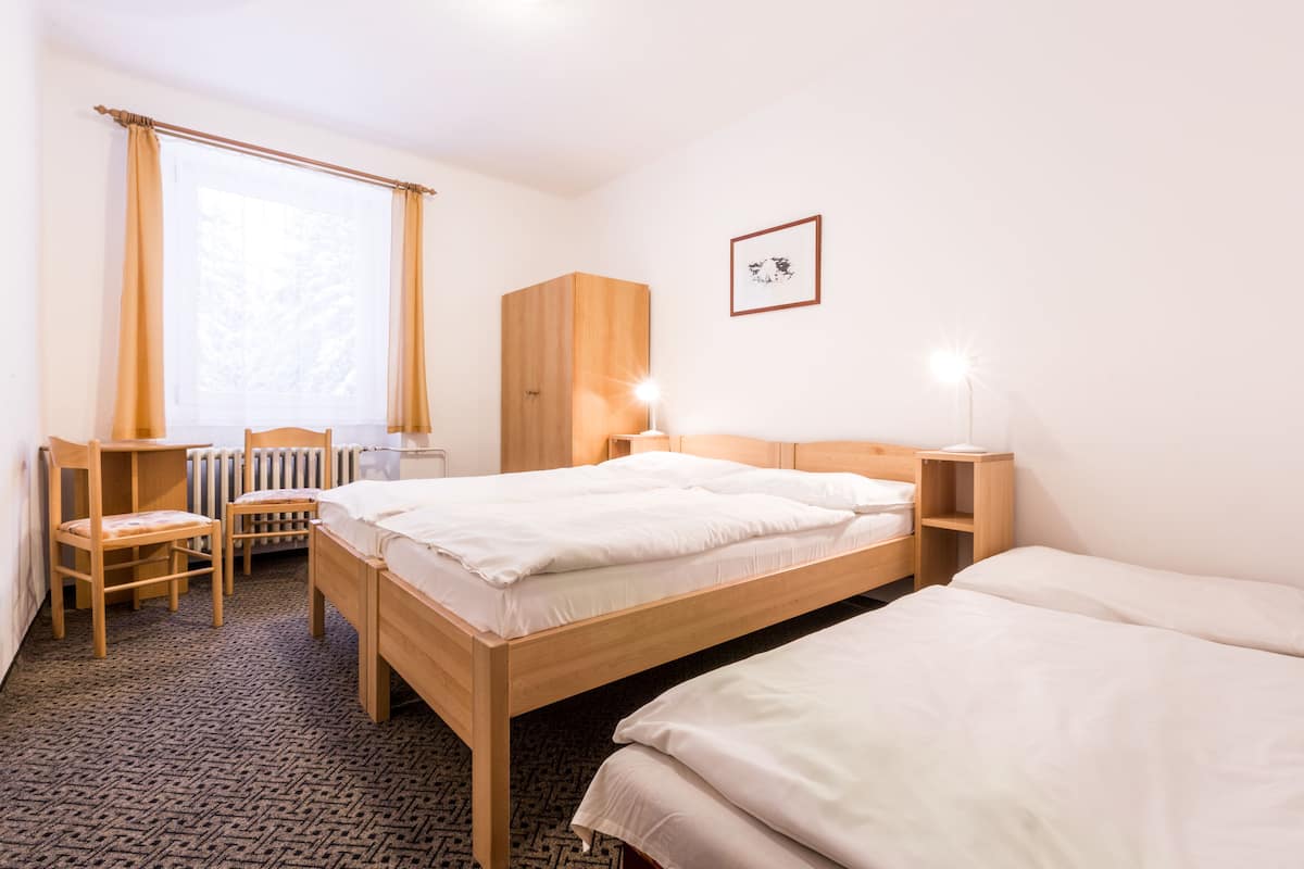 Quarto de hotel com cama de madeira, uma secretária com cadeira, um guarda-roupa e um quadro na parede.