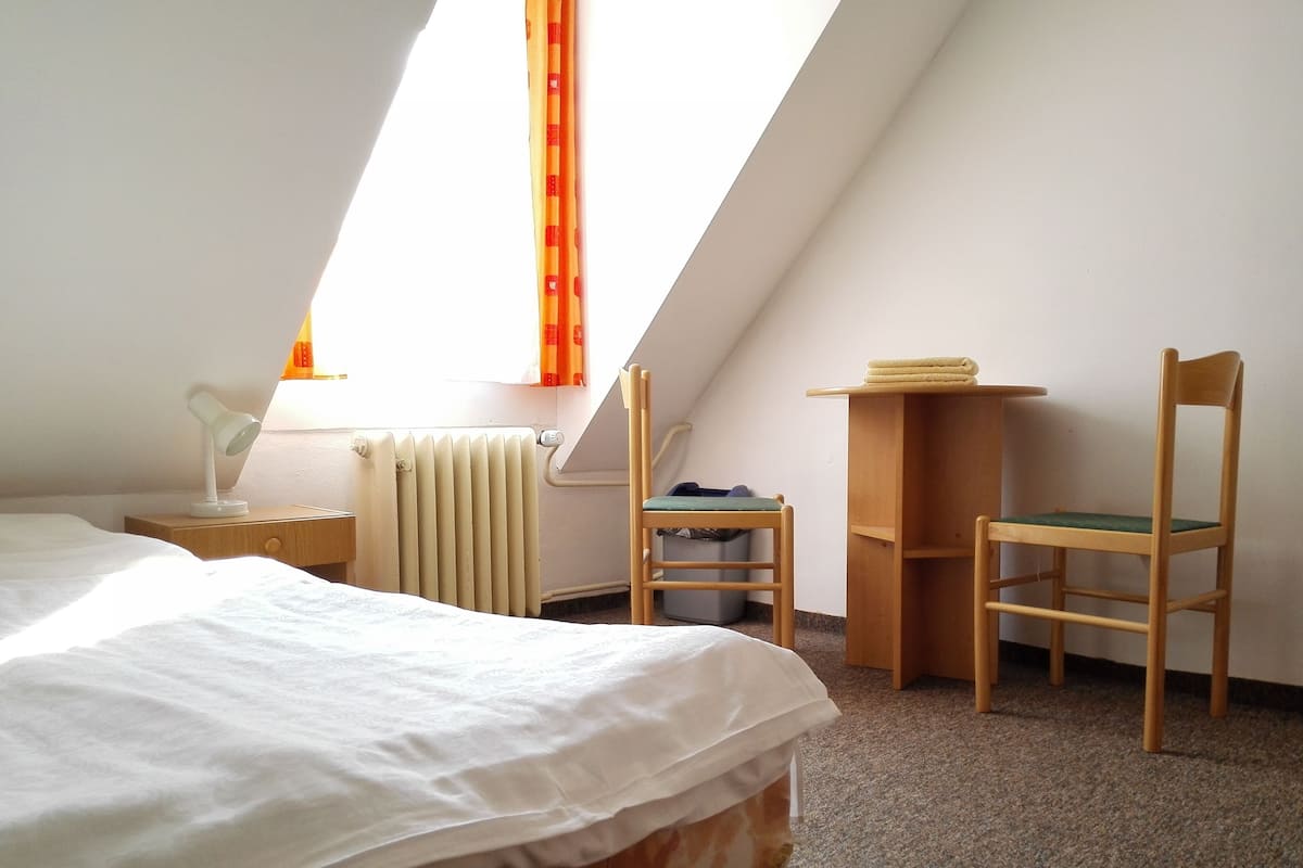 Um quarto com cama, escrivaninha, cadeira, radiador e janela com cortinas.