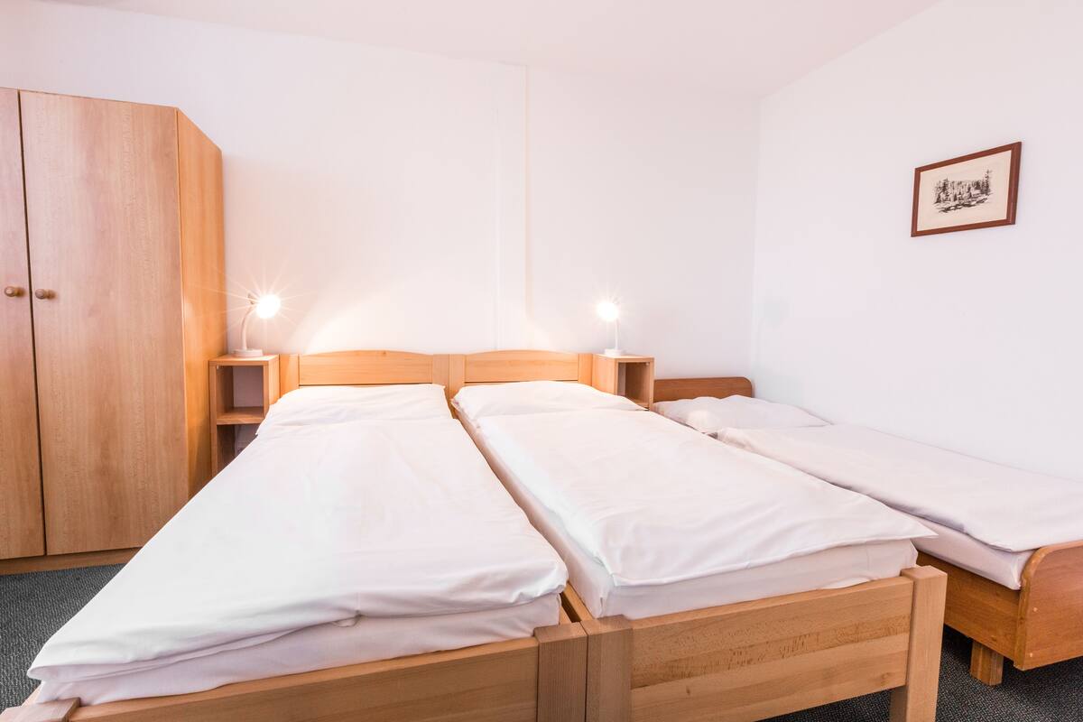 Quarto com duas camas de madeira, um guarda-roupa e uma mesa de cabeceira com abajur.