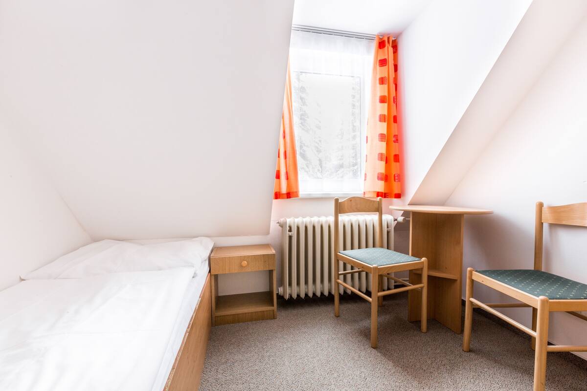 Um quarto com uma cama, uma escrivaninha, uma cadeira e uma janela com cortinas.