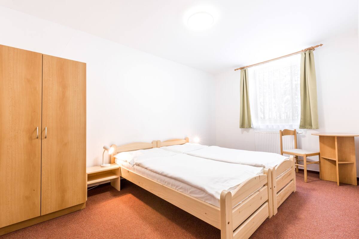 Quarto com cama de casal, guarda-roupa de madeira, escrivaninha e uma cadeira.