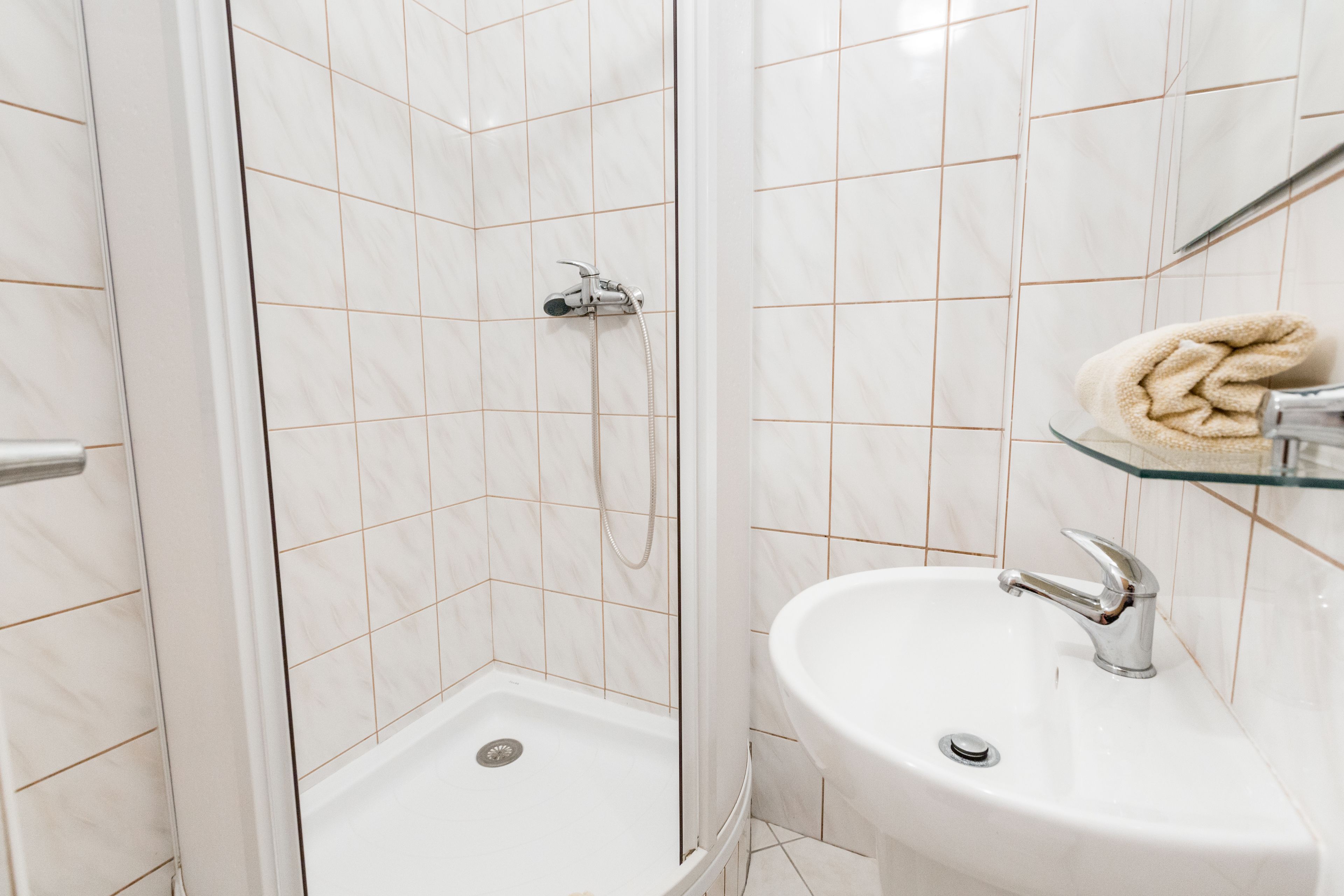 Casa de banho com chuveiro, pia e um prateleira de vidro com uma toalha.