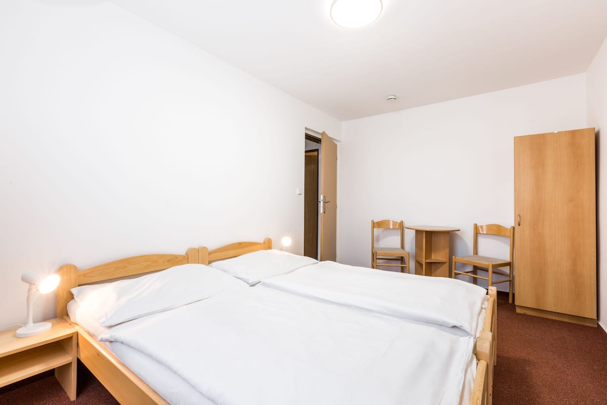 Quarto com duas camas de solteiro, guarda-roupa de madeira, escrivaninha, duas cadeiras e abajur.