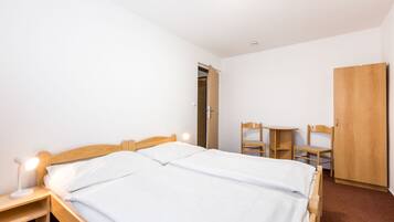 Quarto com duas camas de solteiro, guarda-roupa de madeira, escrivaninha, duas cadeiras e abajur.