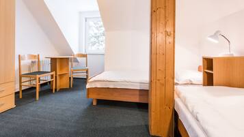 Quarto com teto inclinado, cama, escrivaninha, cadeira e radiador.