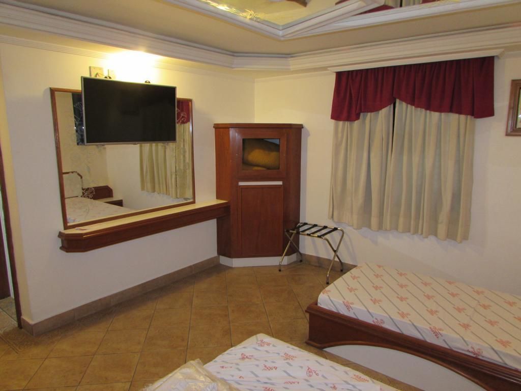 Quarto com cama, televisão na parede, armário de madeira e janela com cortinas.