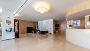 Um hall de hotel moderno com uma mesa de recepção, área de estar e um lustre grande.