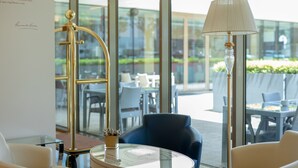 Um hall de hotel moderno com divisória de vidro, assentos confortáveis, uma luminária e vista para o pátio externo.