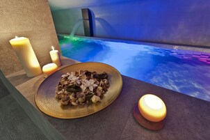 Espaço de spa com hidromassagem, velas e um prato de flores secas sobre superfície texturizada.