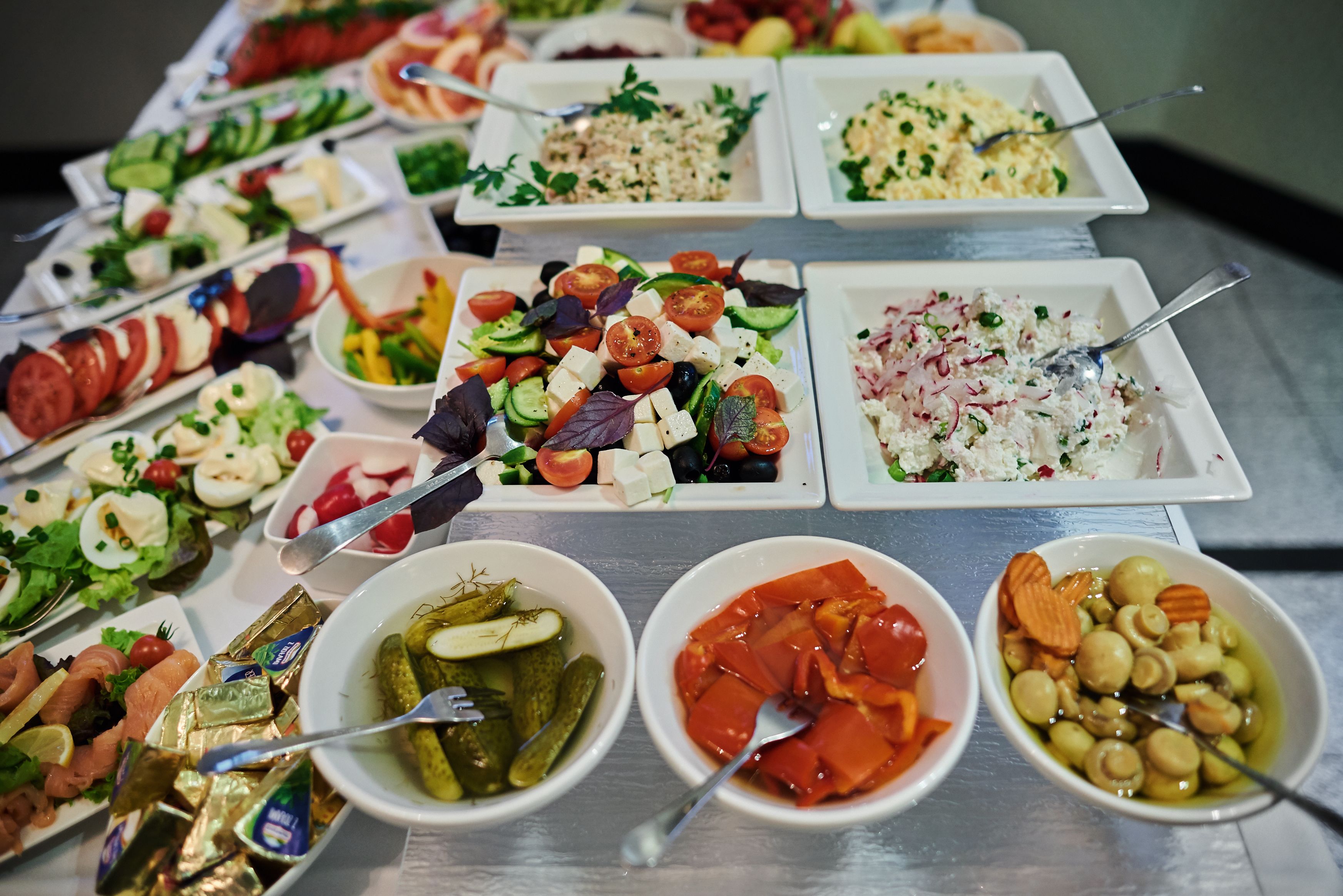 Buffet com diversos pratos, incluindo saladas, queijos e picles.