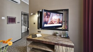 Quarto de hotel com televisão de tela plana na parede, mesa de consola de madeira com um bloco de notas, um copo e uma garrafa.