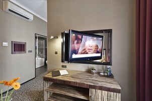 Quarto de hotel com televisão de tela plana na parede, mesa de consola de madeira com um bloco de notas, um copo e uma garrafa.