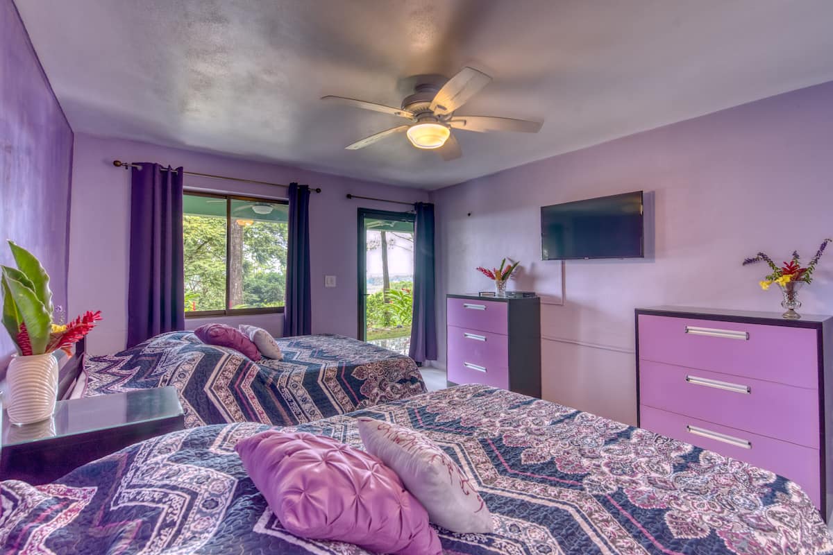 Quarto com cama, penteadeira, televisão e janela com cortinas.