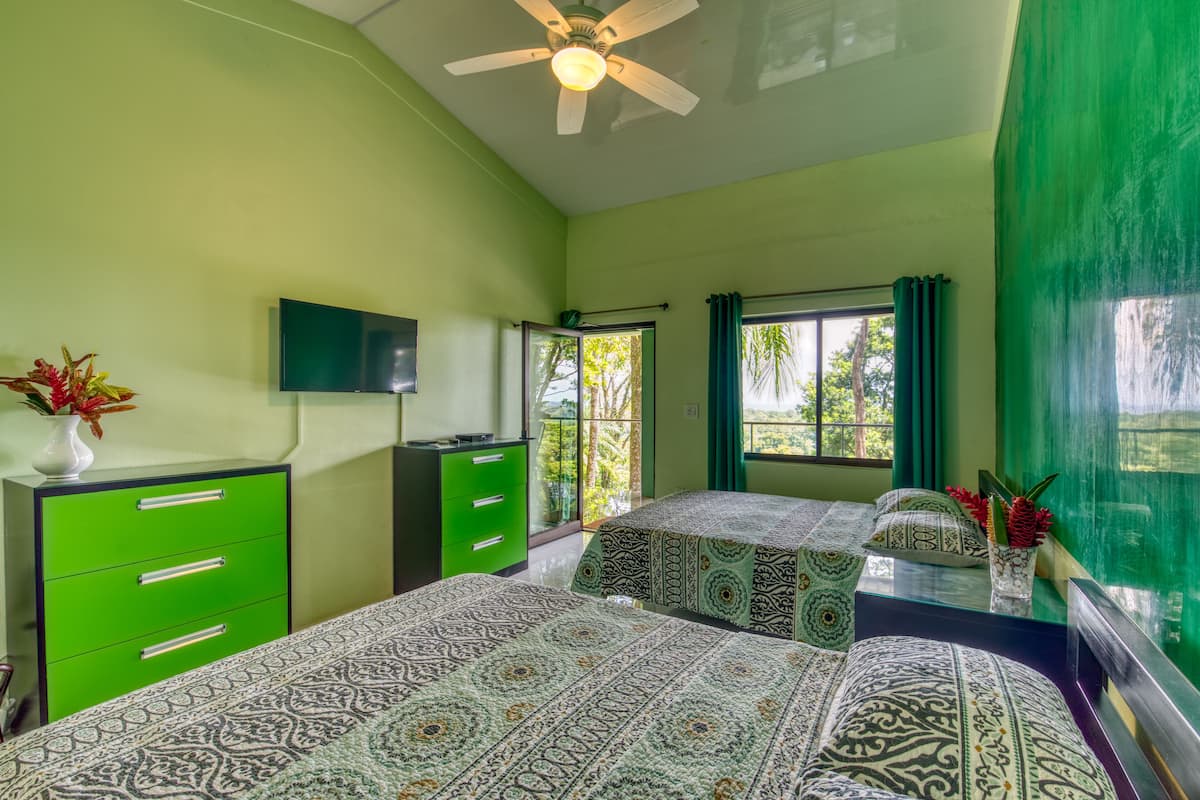 Quarto com duas camas, televisão, escrivaninha e janela com cortinas.