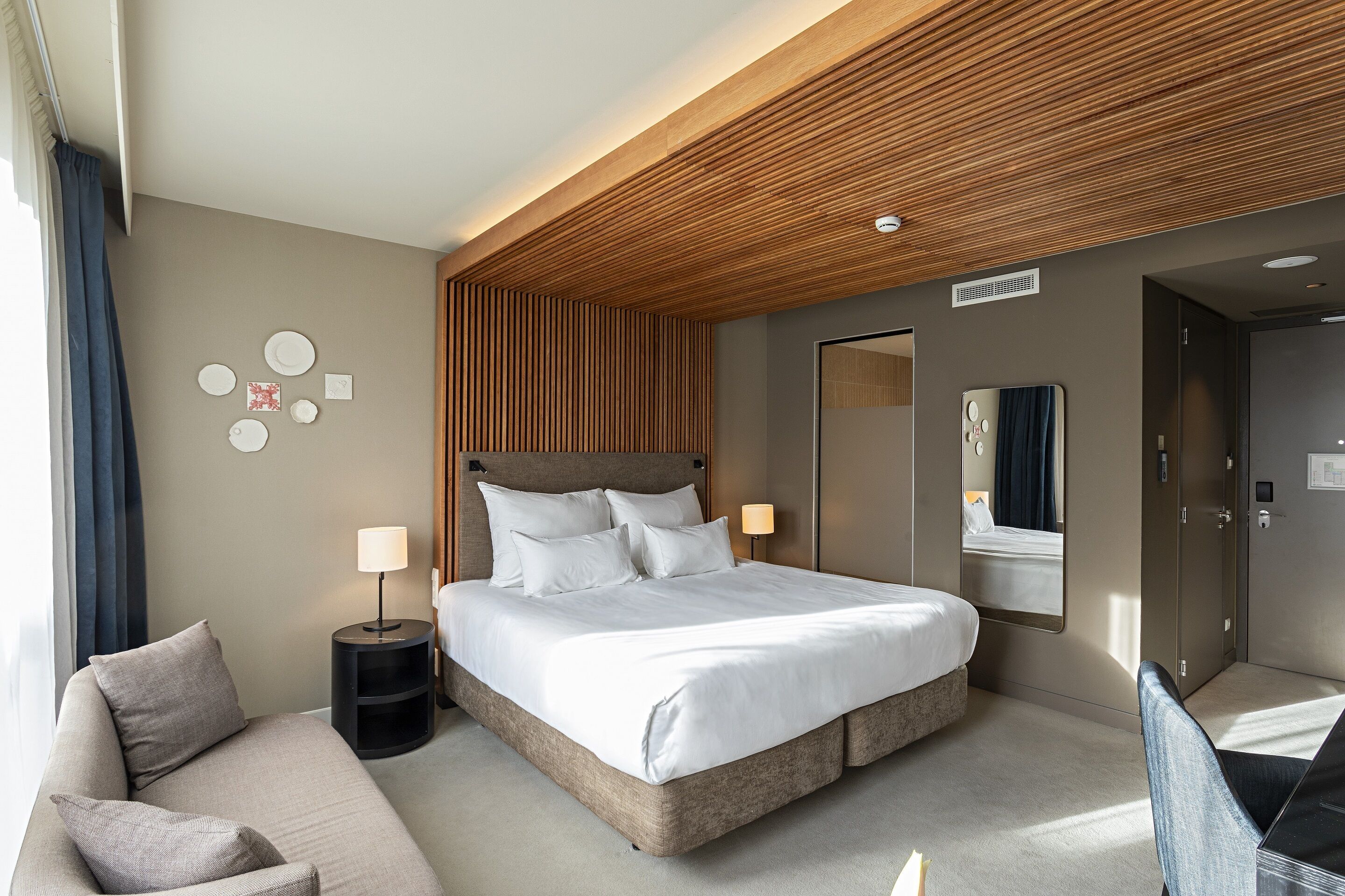 Quarto de hotel moderno com uma cama grande, um sofá, uma escrivaninha e um espelho.