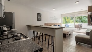 Cozinha moderna com ilha central, banquetas de bar e área de refeições com cama e assentos.