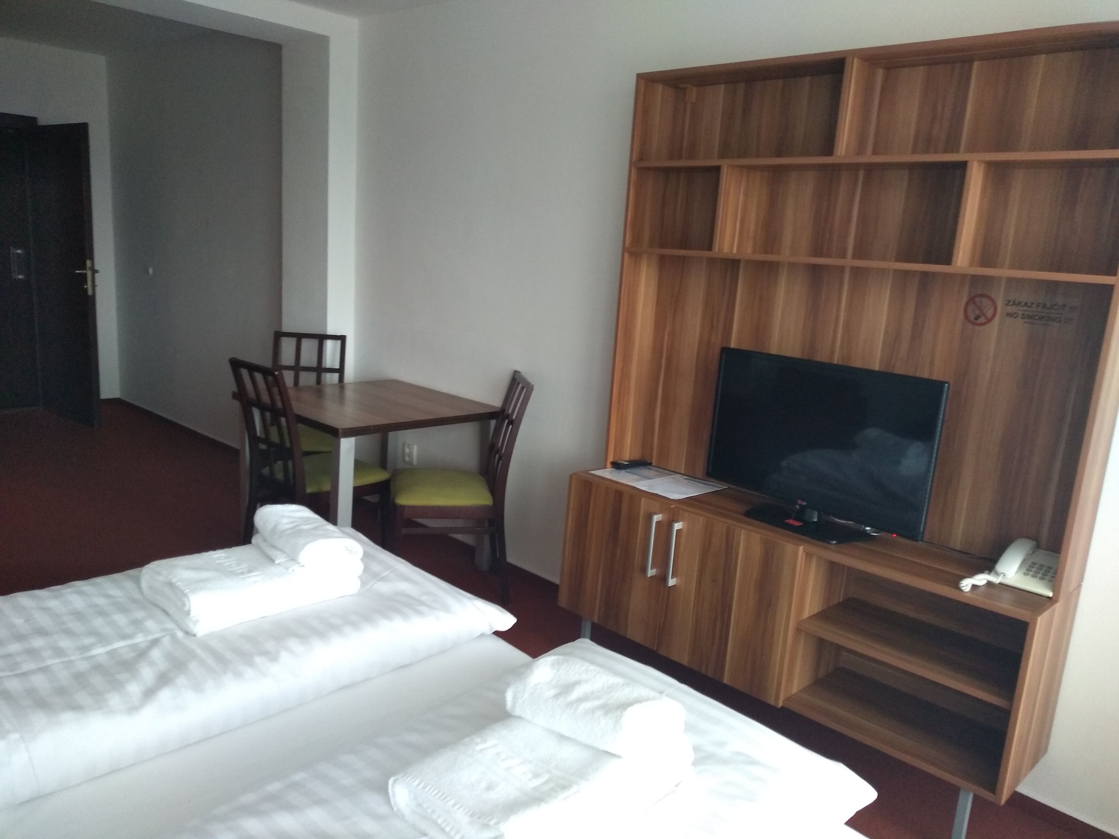 Quarto de hotel com duas camas, um móvel de televisão de madeira, uma escrivaninha com cadeiras e um telefone.