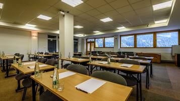 Sala de conferências com várias mesas, cadeiras e garrafas de água.