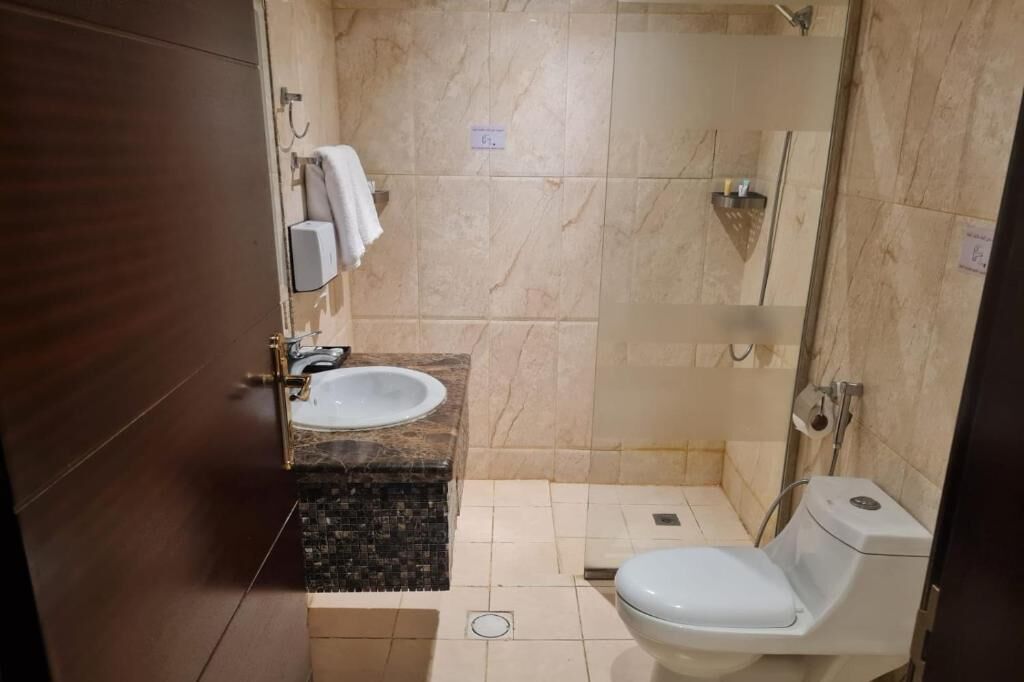 Casa de banho com chuveiro, sanita, lavatório e dispensador de toalhas.