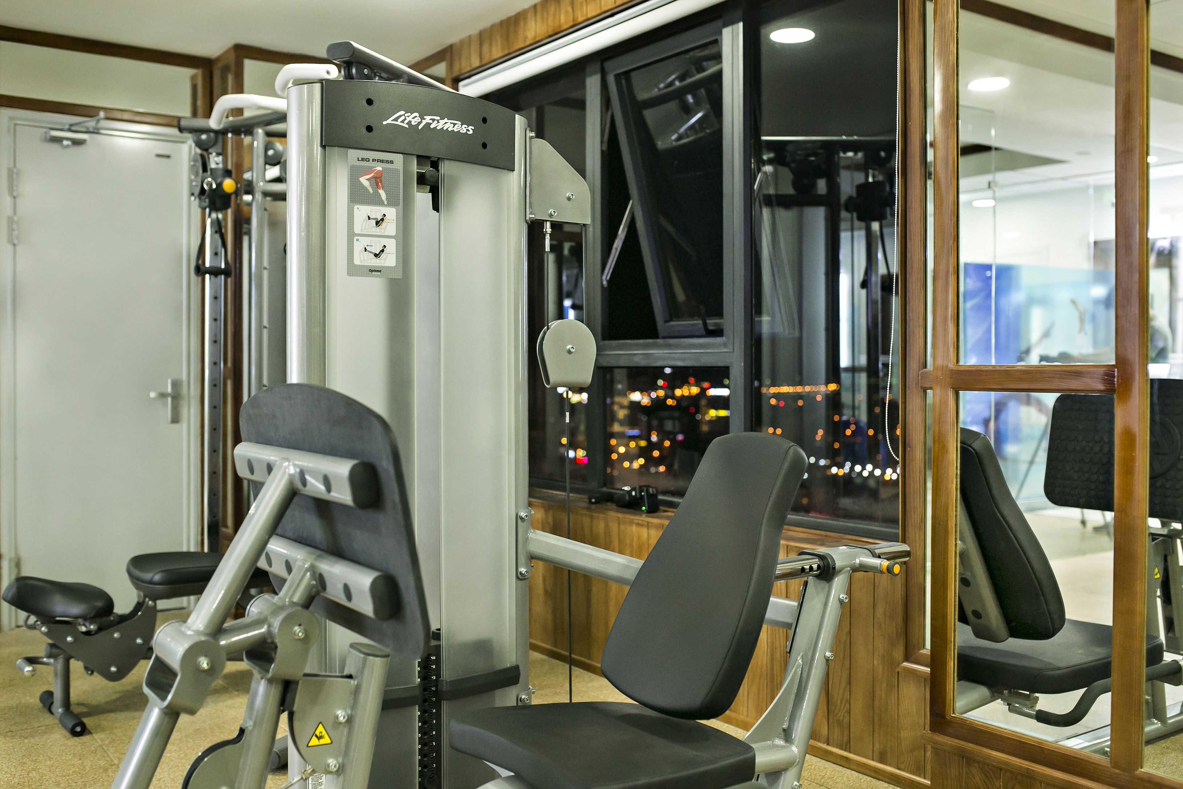 Uma academia com equipamentos de ginástica, uma janela com vista para luzes da cidade e uma porta.