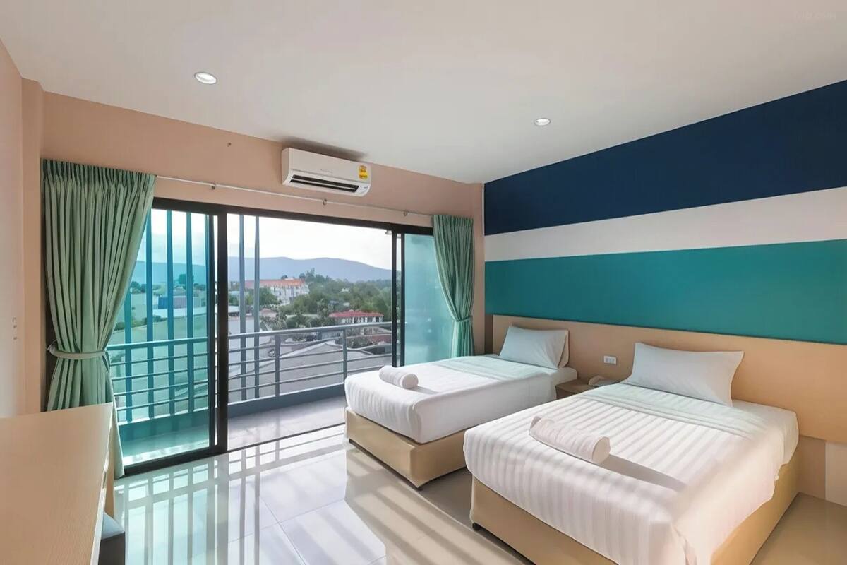 Quarto de hotel com duas camas, uma janela grande com cortinas, ar condicionado e vista para a paisagem urbana.