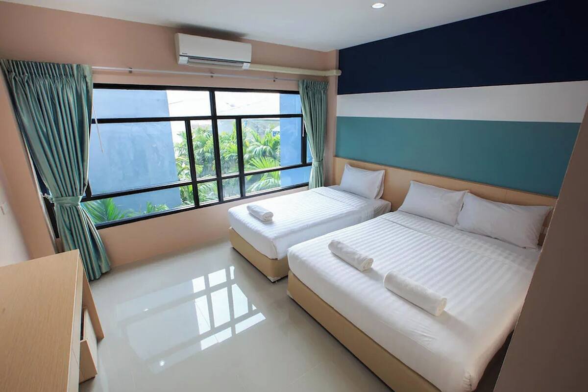 Quarto de hotel com duas camas, janela com cortinas e vista para o verde lá fora.