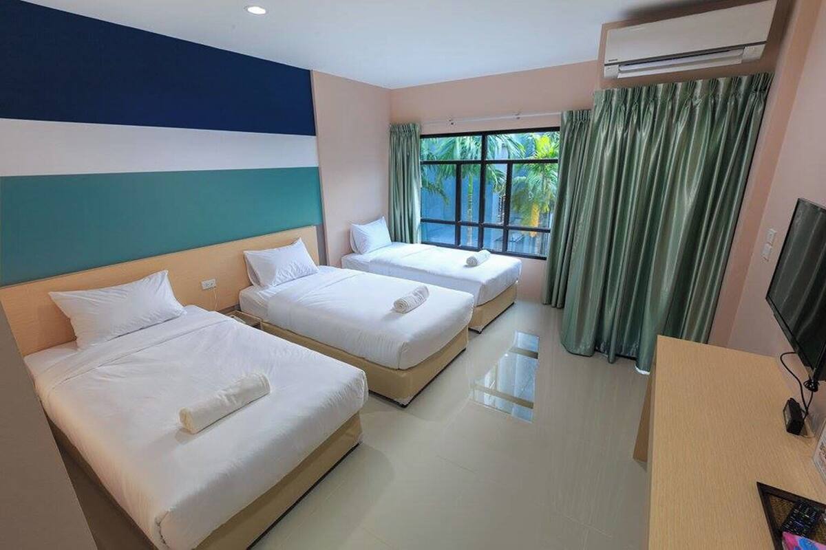 Quarto de hotel com duas camas de solteiro, uma escrivaninha com computador e uma janela com cortinas.
