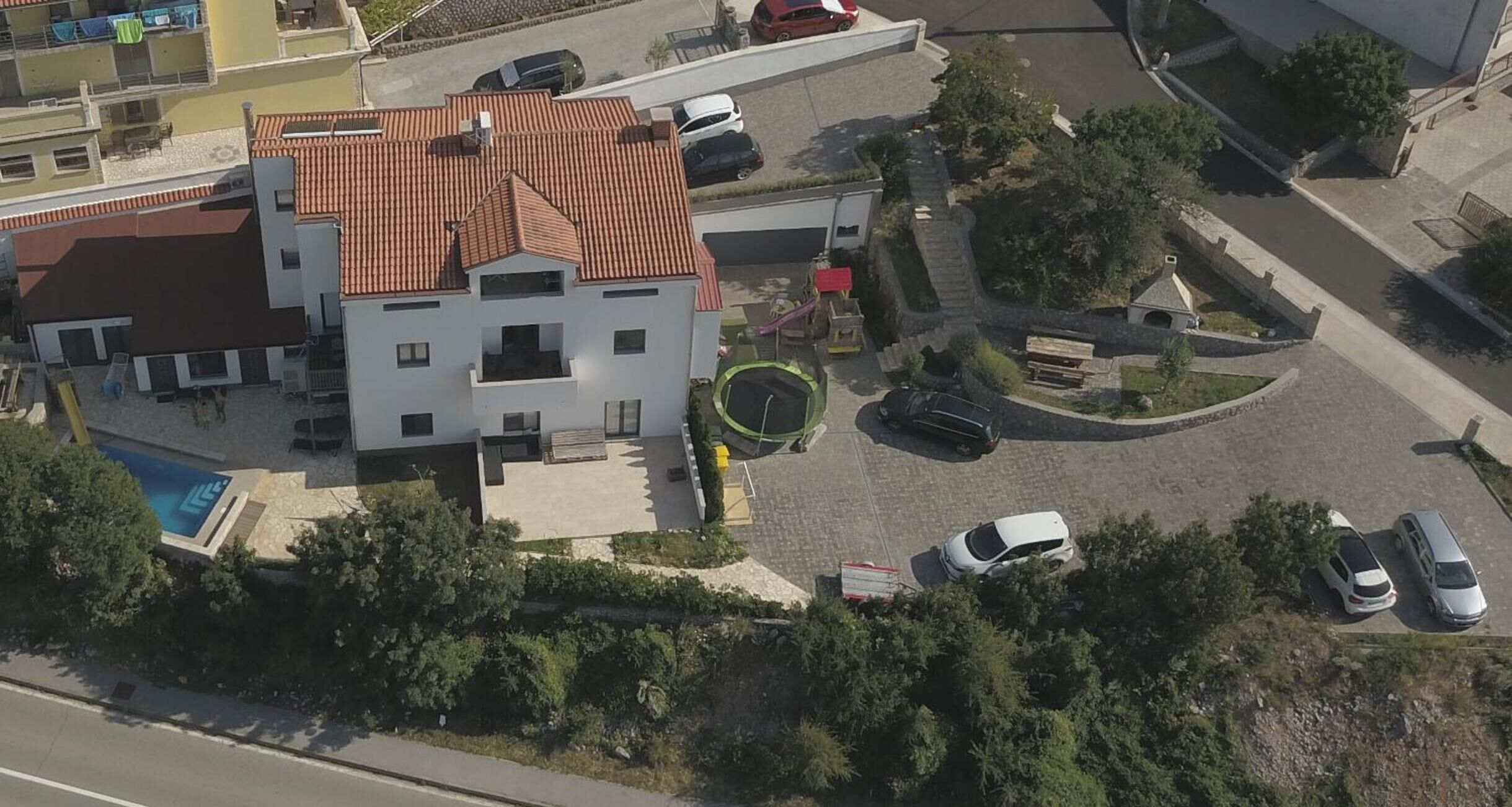 Vista aérea de uma área residencial com uma casa moderna de dois andares, piscina e estacionamento com vários carros.