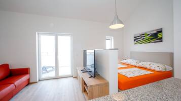 Quarto moderno com um sofá vermelho, uma cama com roupa de cama laranja, uma televisão sobre um suporte de madeira e um quadro na parede.