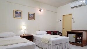 Quarto de hotel com duas camas, uma mesa de cabeceira com abajur, um pequeno frigorífico e ar condicionado fixado na parede.