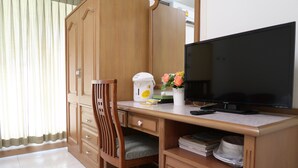 Uma escrivaninha de madeira com uma televisão, uma cadeira e uma pequena mesa com cafeteira e flores.