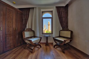 Quarto com duas cadeiras de madeira, uma mesinha e vista para uma mesquita através de uma janela.