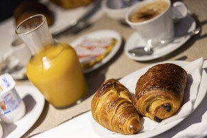 Uma mesa com croissants, um copo de sumo de laranja e uma chávena de café.
