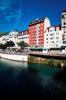 Hotel à beira-rio com vários andares, fachada em vermelho e branco marcante e vista para o rio.
