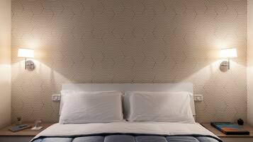 Cama bem arrumada com roupa de cama branca e azul, duas luminárias de mesa e uma parede estampada.