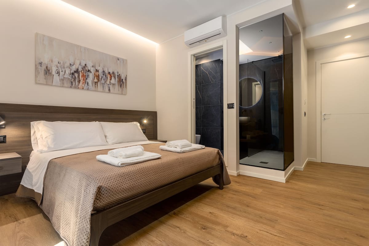 Quarto moderno com uma cama grande, um quadro na parede e uma porta de vidro deslizante para um banheiro.