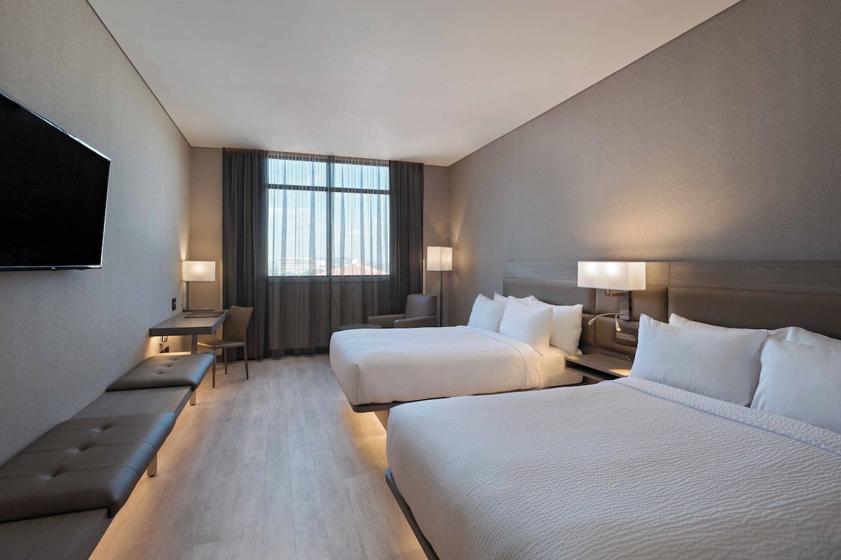Quarto de hotel com duas camas, uma escrivaninha, uma cadeira e uma televisão.