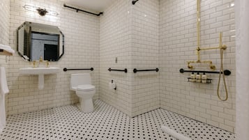 Um banheiro com azulejos brancos tipo metrô, vaso sanitário branco, pia com torneira dourada e chuveiro com chuveiro dourado.