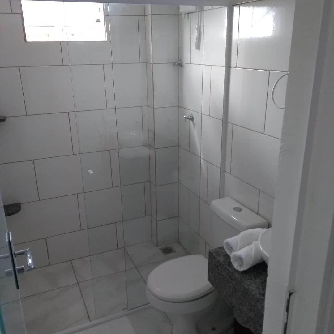 Um banheiro pequeno com azulejos, chuveiro, vaso sanitário e pia com toalha.
