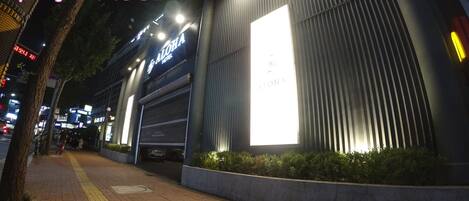 Um edifício com uma grande placa iluminada com a inscrição "ALOHA HOTEL" e um estacionamento adjacente.