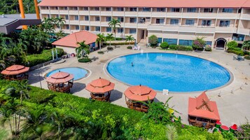 Um hotel com uma piscina central grande, piscinas menores ao redor e várias cabanas sobre a água.
