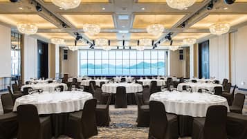 Uma sala de banquetes com mesas redondas, cadeiras pretas e lustres.