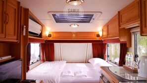 Interior aconchegante de uma motorhome, com cama, cozinha compacta e ventoinha no teto.