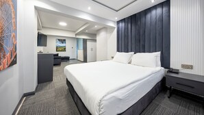 Quarto de hotel moderno com uma cama grande, uma escrivaninha e vista para a paisagem urbana.