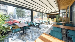 Um café moderno com mesas de madeira e cadeiras cor de verde-água, grandes janelas com vista para a rua e teto de madeira.