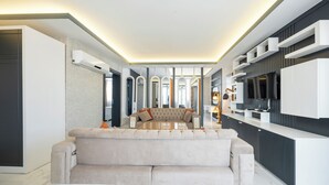 Uma sala moderna com um sofá bege grande, uma área de jantar com mesa de vidro e unidades de entretenimento embutidas.
