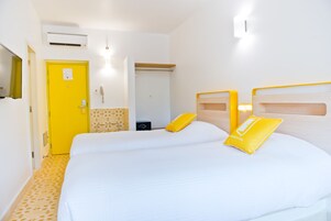 Quarto de hotel com duas camas, uma porta amarela, um espelho e uma pequena mesa de cabeceira.
